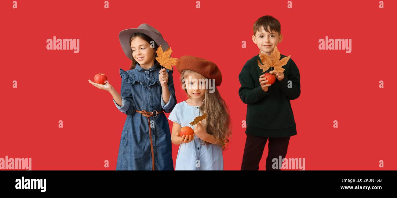 Cute little children holding autumn leaves and apples on red background ...