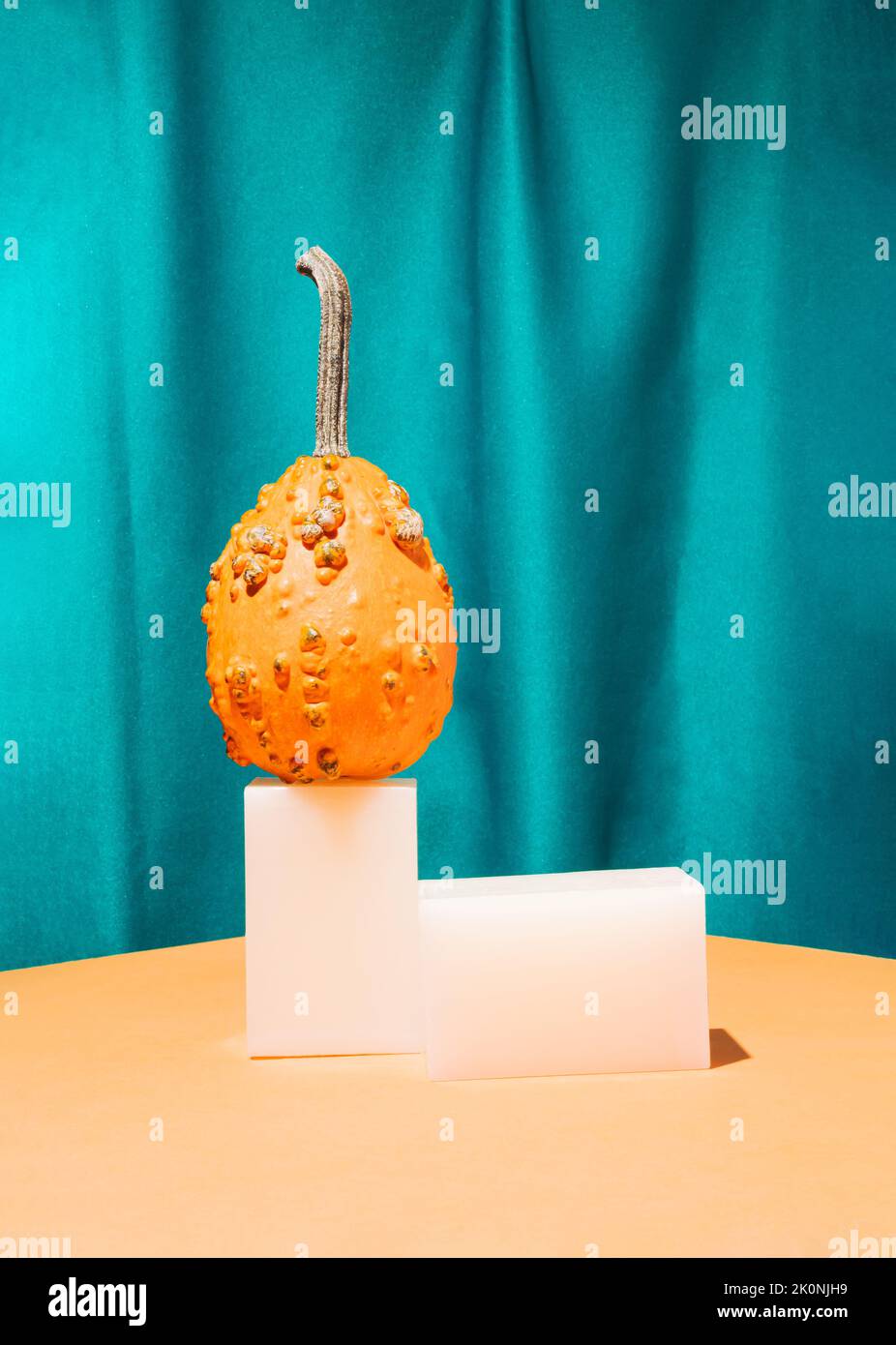 Still life with organic orange gourd and white podium with silk blue ...