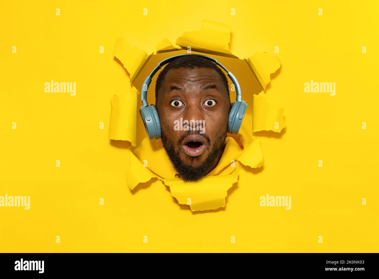 Emotional black man listening favorite music via headphones and staring at camera through hole ...