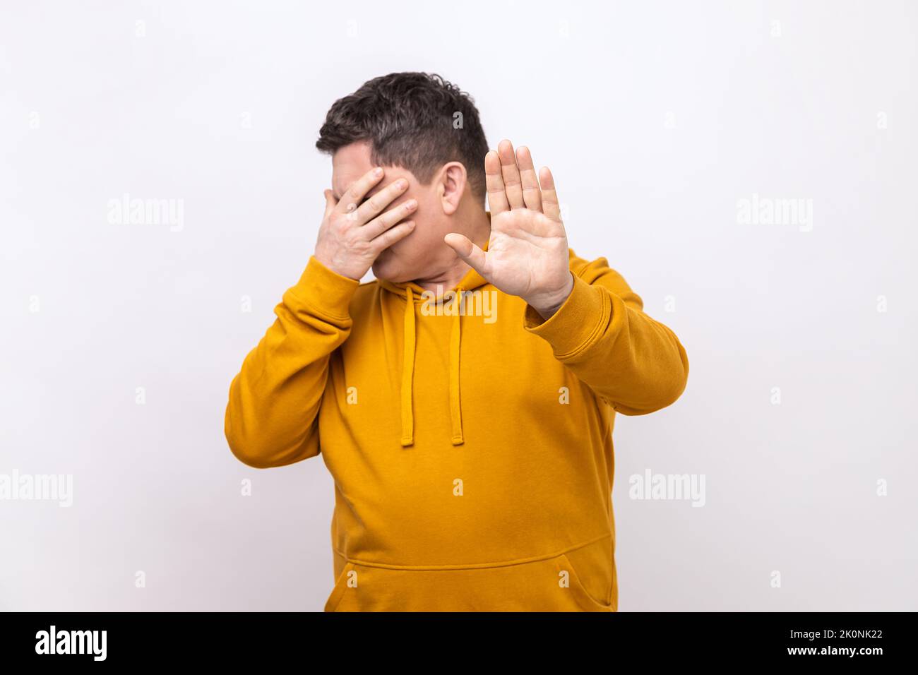 Portrait of confused man covering eyes and raising hand to stop ...
