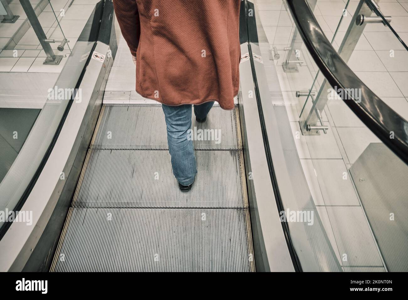 Caucasian woman in red jacket goes down on an iron escalator in mall ...