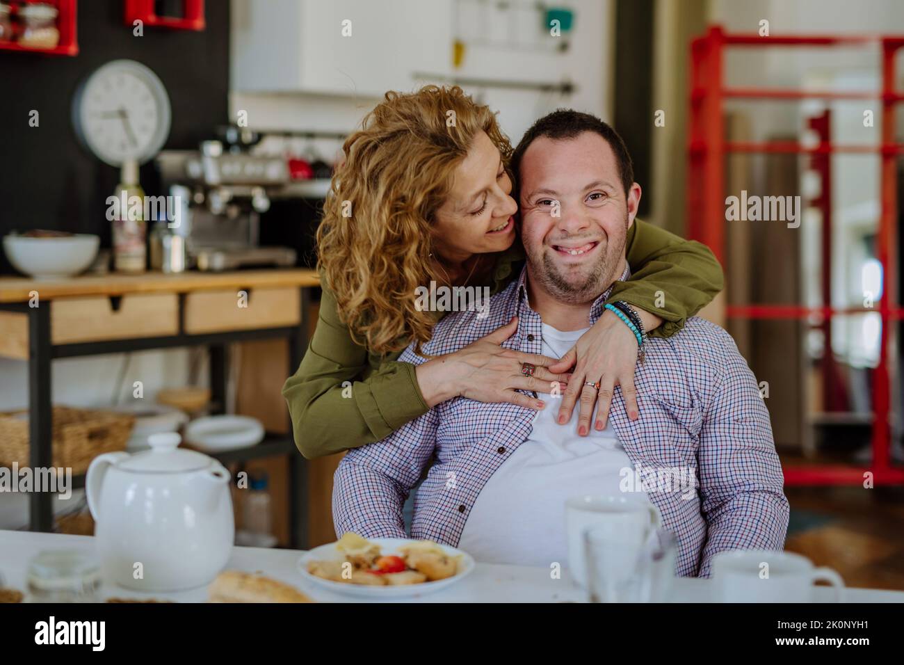 Portrait of happy young man with Down syndrome with his mother at home ...