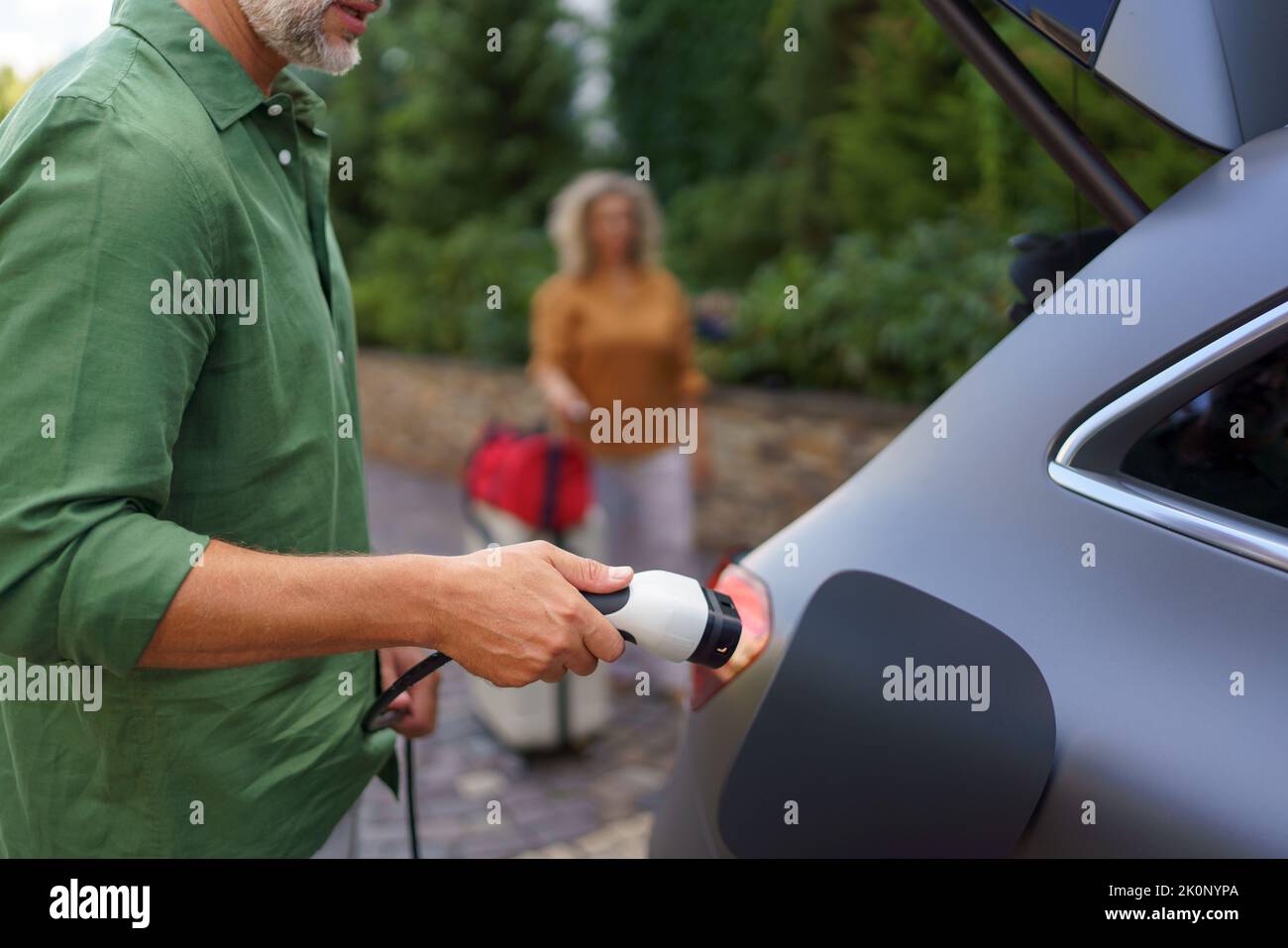 Man holding power supply cable, while his wife waiting for car charging ...