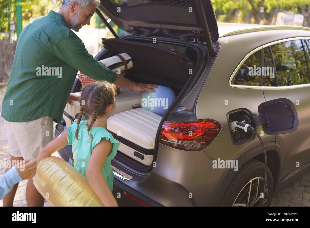 Family with little children loading car and waiting for charging car ...