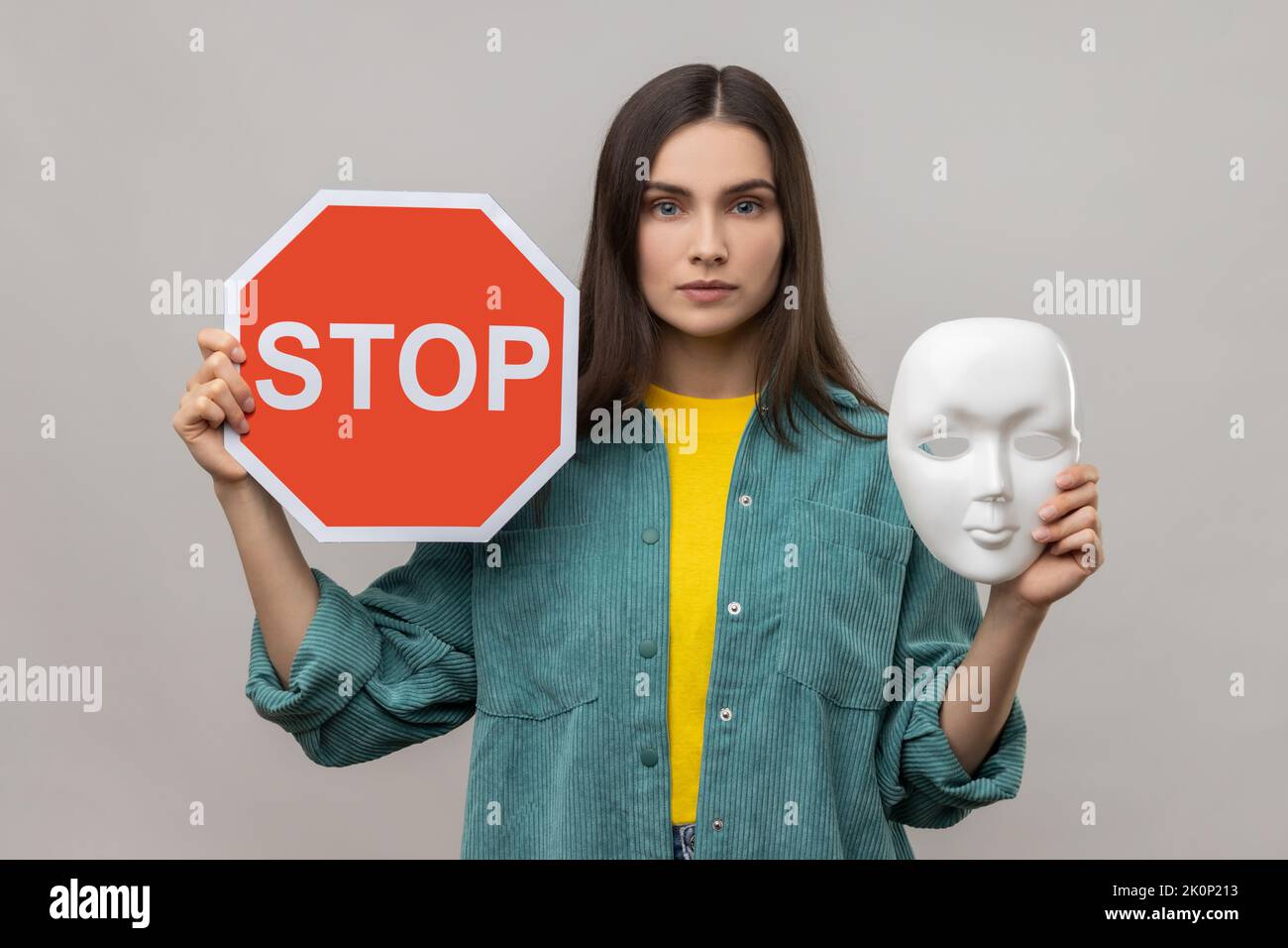 Portrait of serious dark haired woman holding red stop sign and white ...