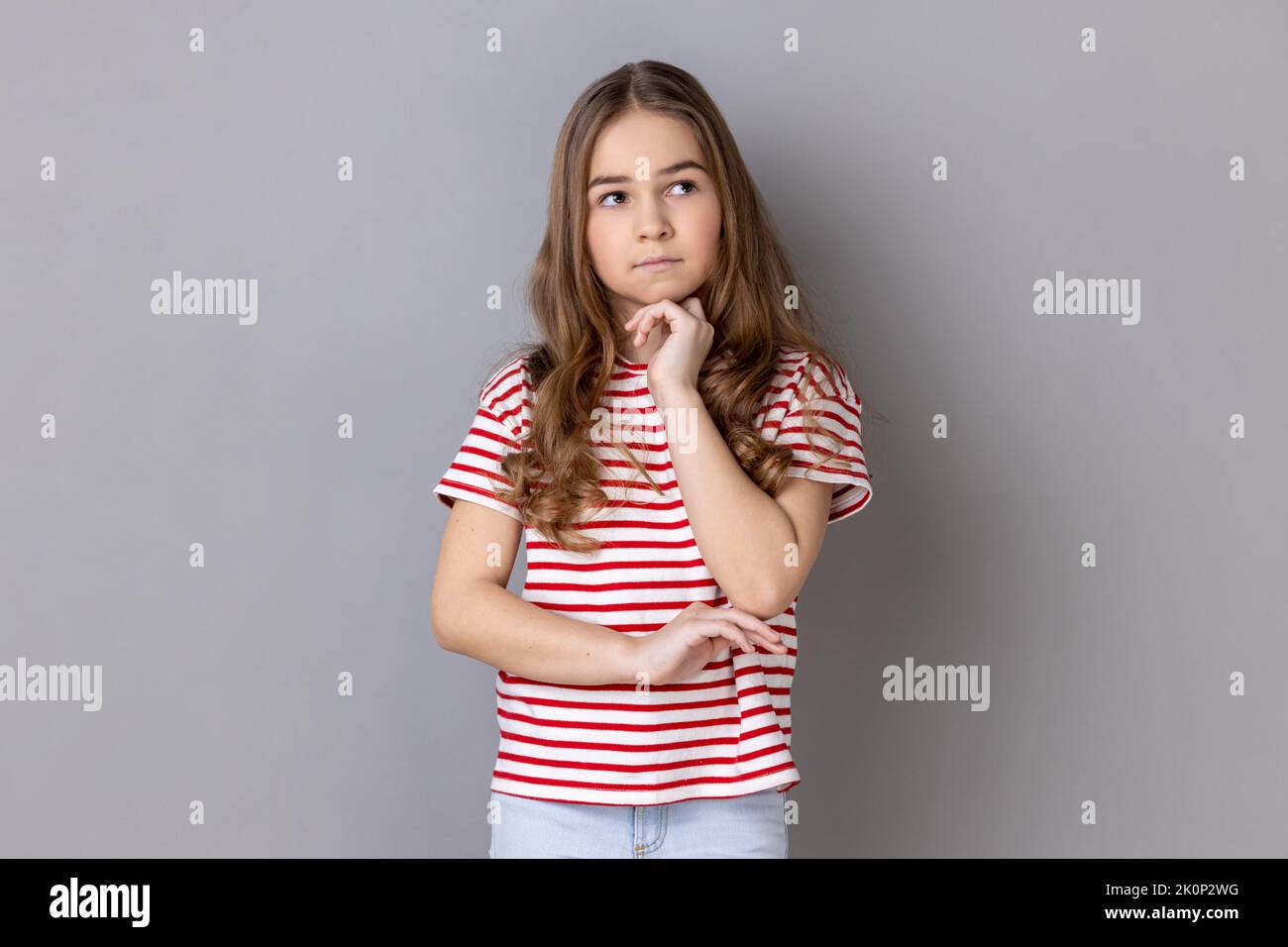 Portrait of thoughtful pensive little dark haired girl wearing striped ...