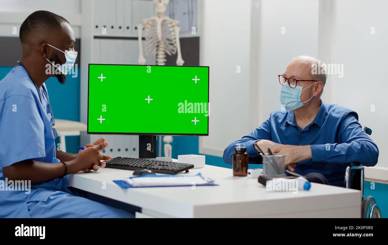 Nurse and senior man with disability looking at greenscreen on monitor ...