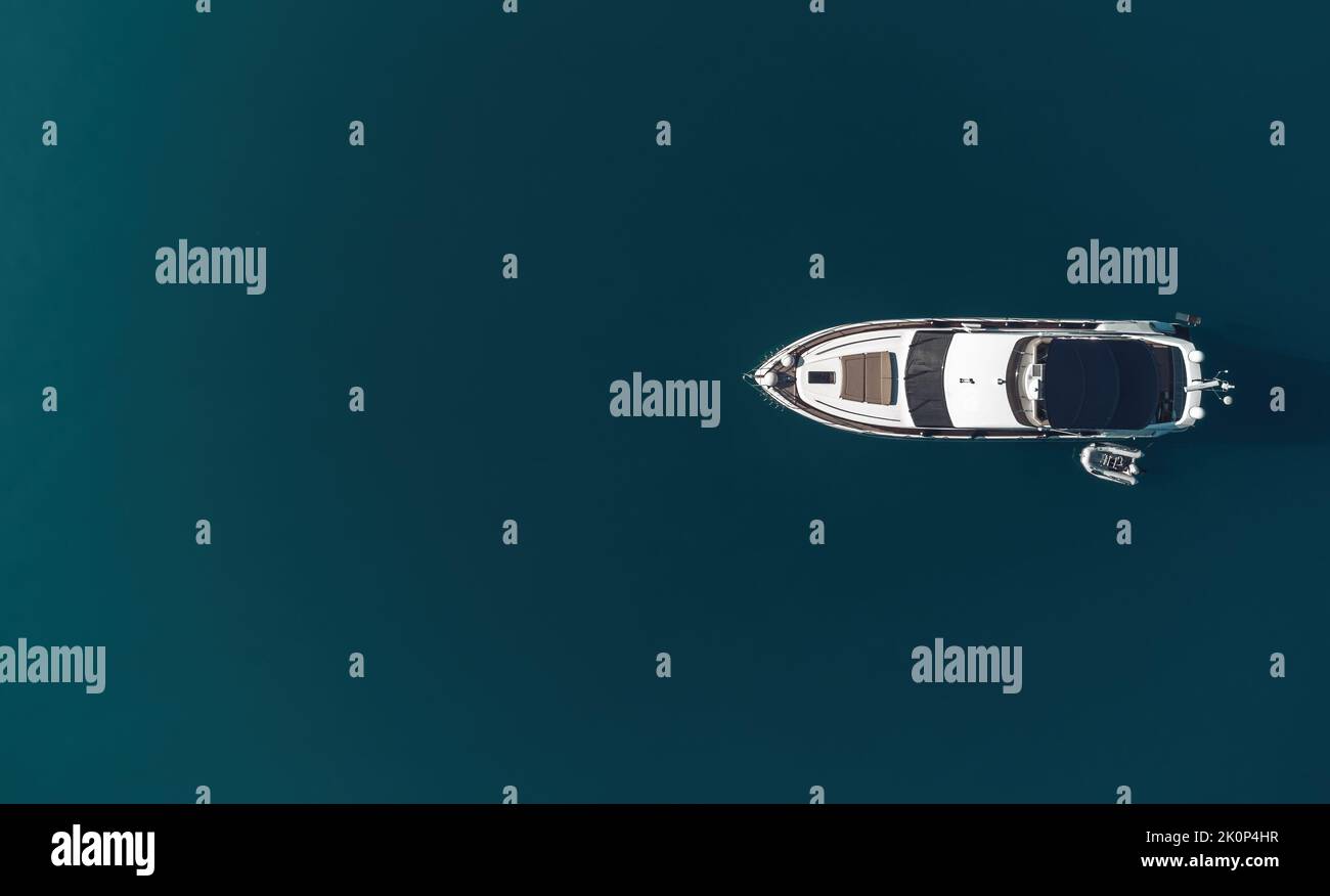 Aerial yacht on calm sea. Luxury cruise trip. View from above of white boat on deep blue water ...
