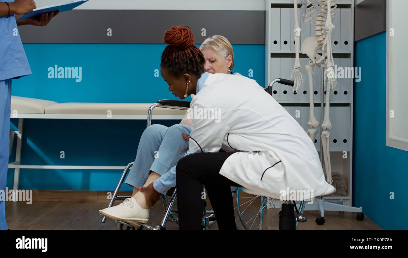 Female osteopath and nurse examining patient in wheelchair, doing ...