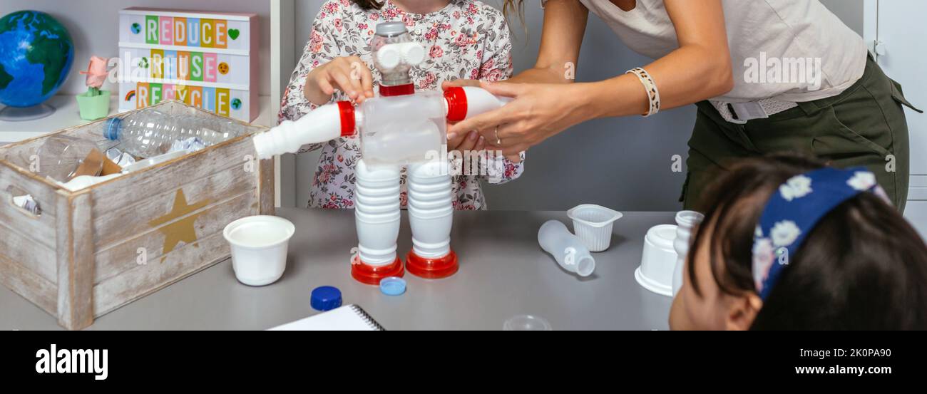 Teacher helping to girl make recycled toy robot with plastic packages ...