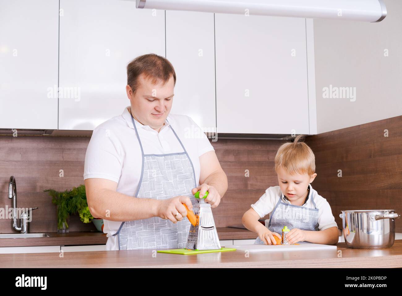 Father cooks with his son, rub carrots on grater at home in the kitchen ...