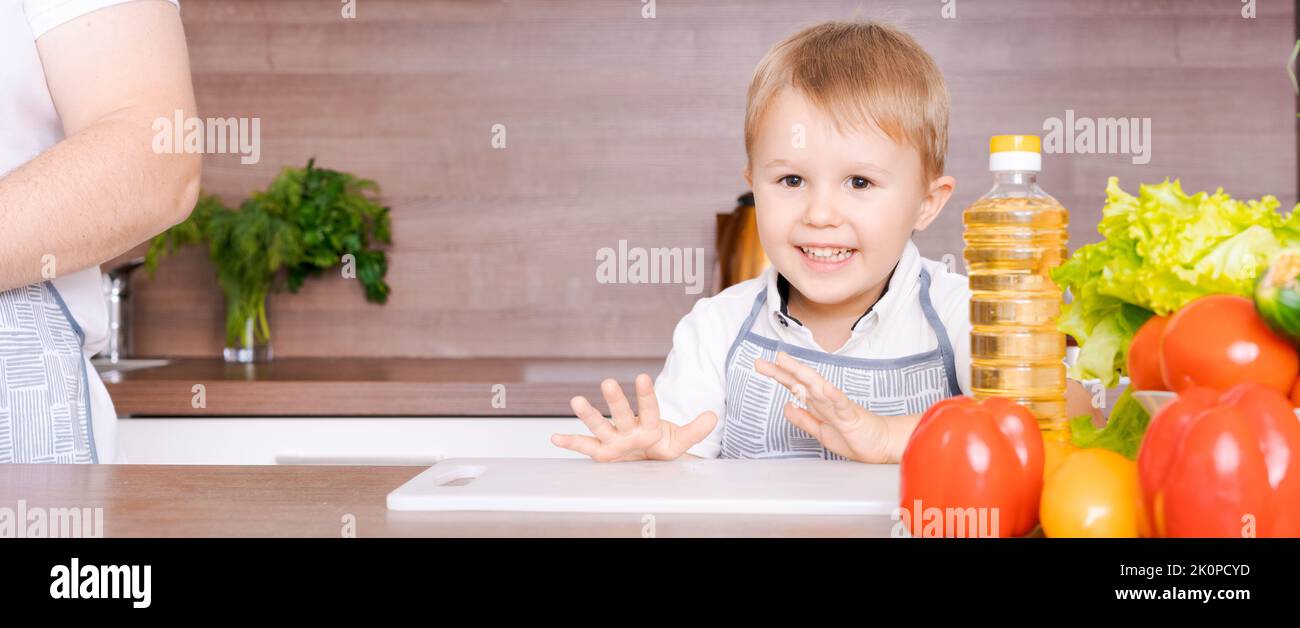Little boy cook and an apron in kitchen smiles, vegetables and ...