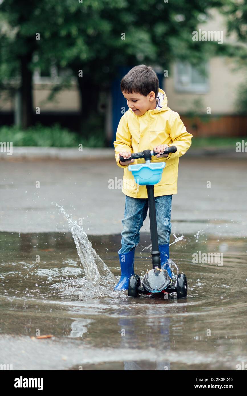 Little boy in raincoat and rubber boots playing in puddle. Fun on ...