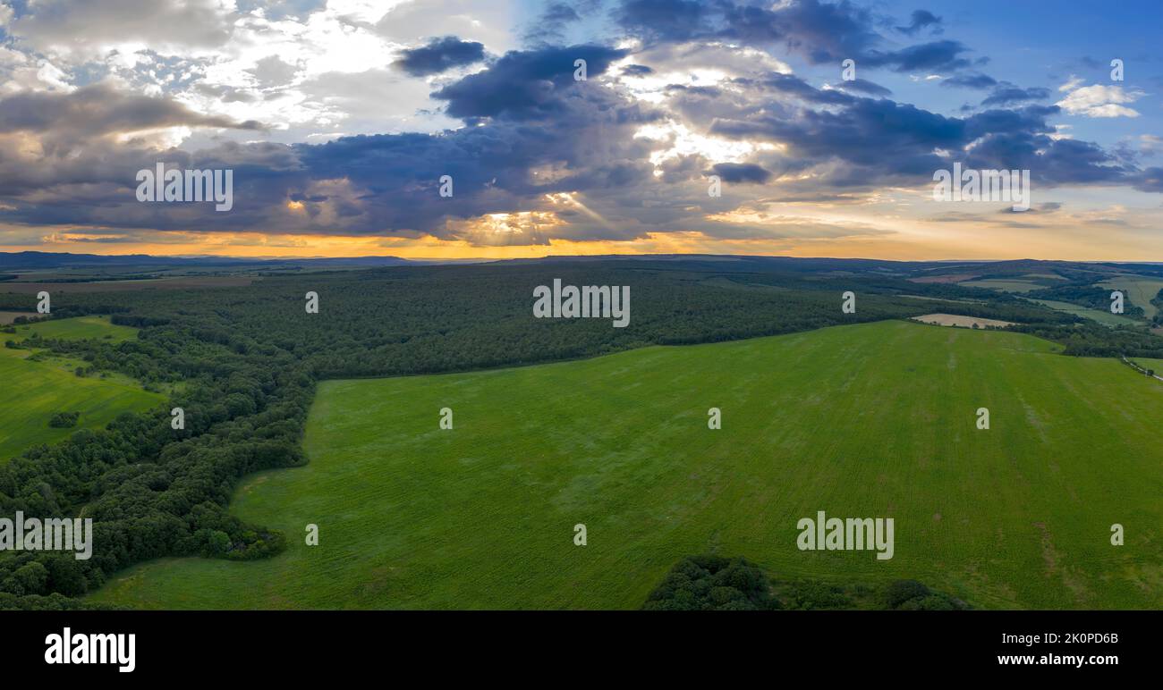 Amazing panoramic view of cloudy sky with sun rays over green field and ...