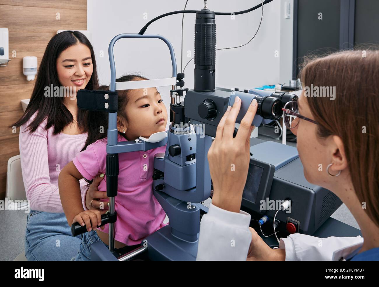 Cute little Asian girl getting eye exam at ophthalmology clinic with optometrist. Checking ...