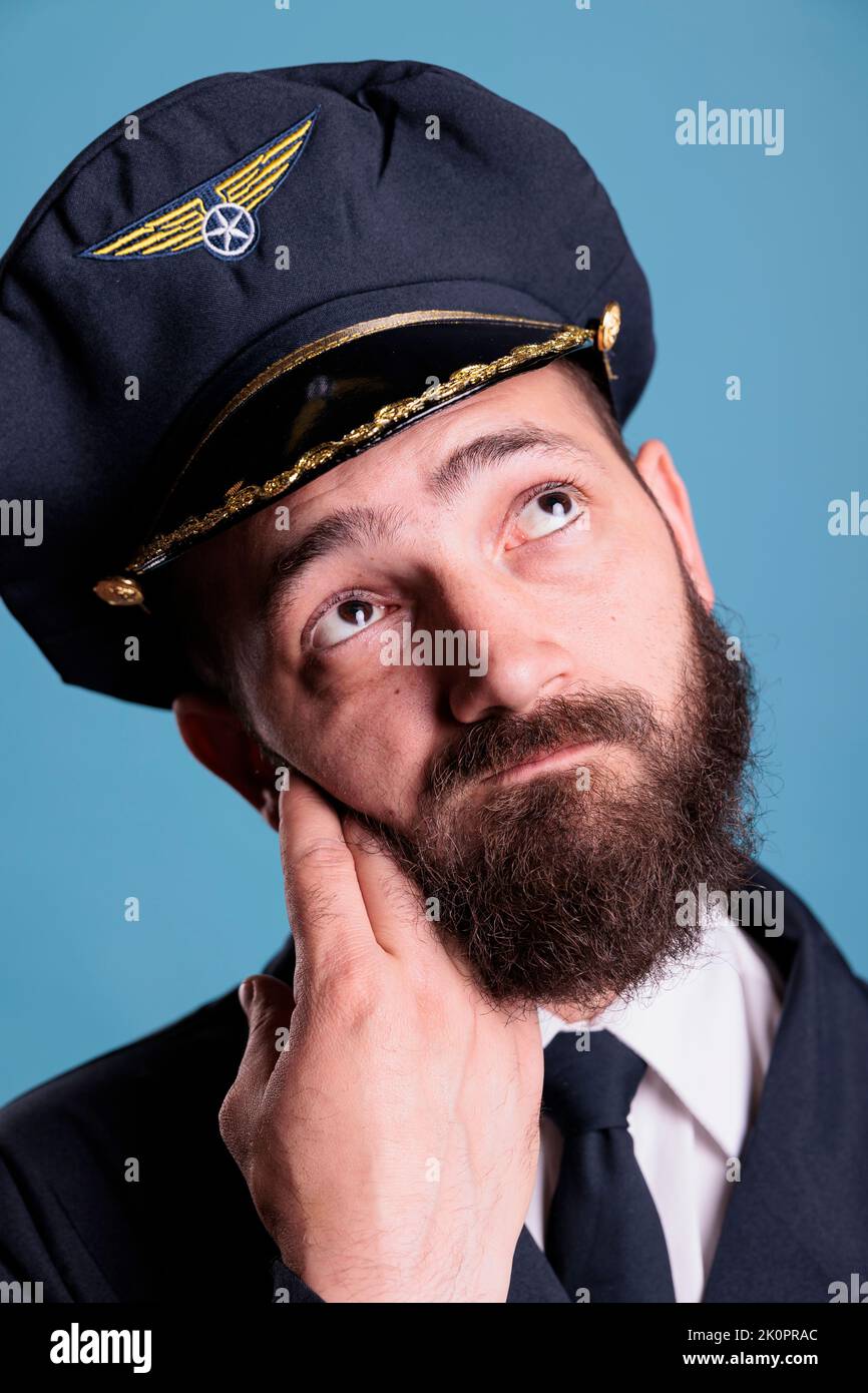 Thoughtful airline pilot in uniform looking upwards, thinking, dreaming ...