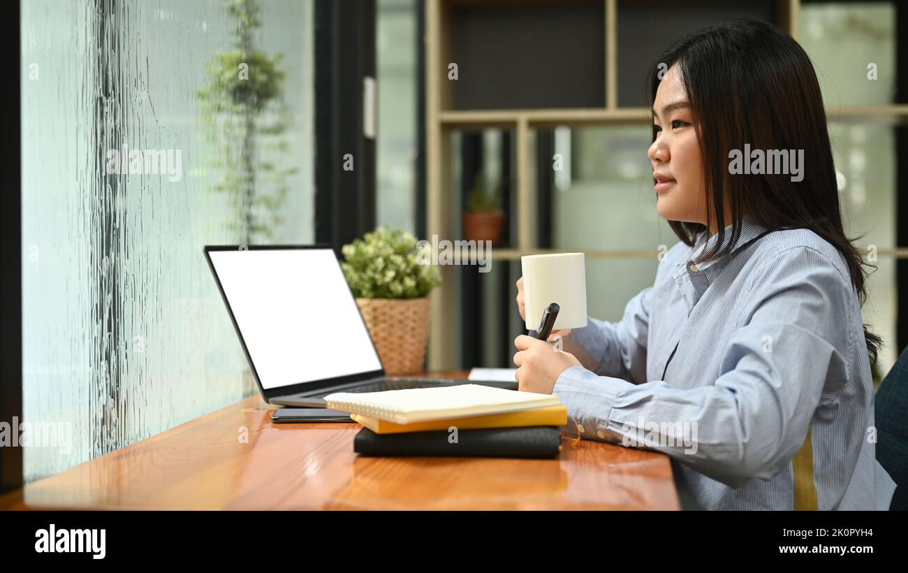 Side view asian woman employee drinking coffee at her workplace and ...