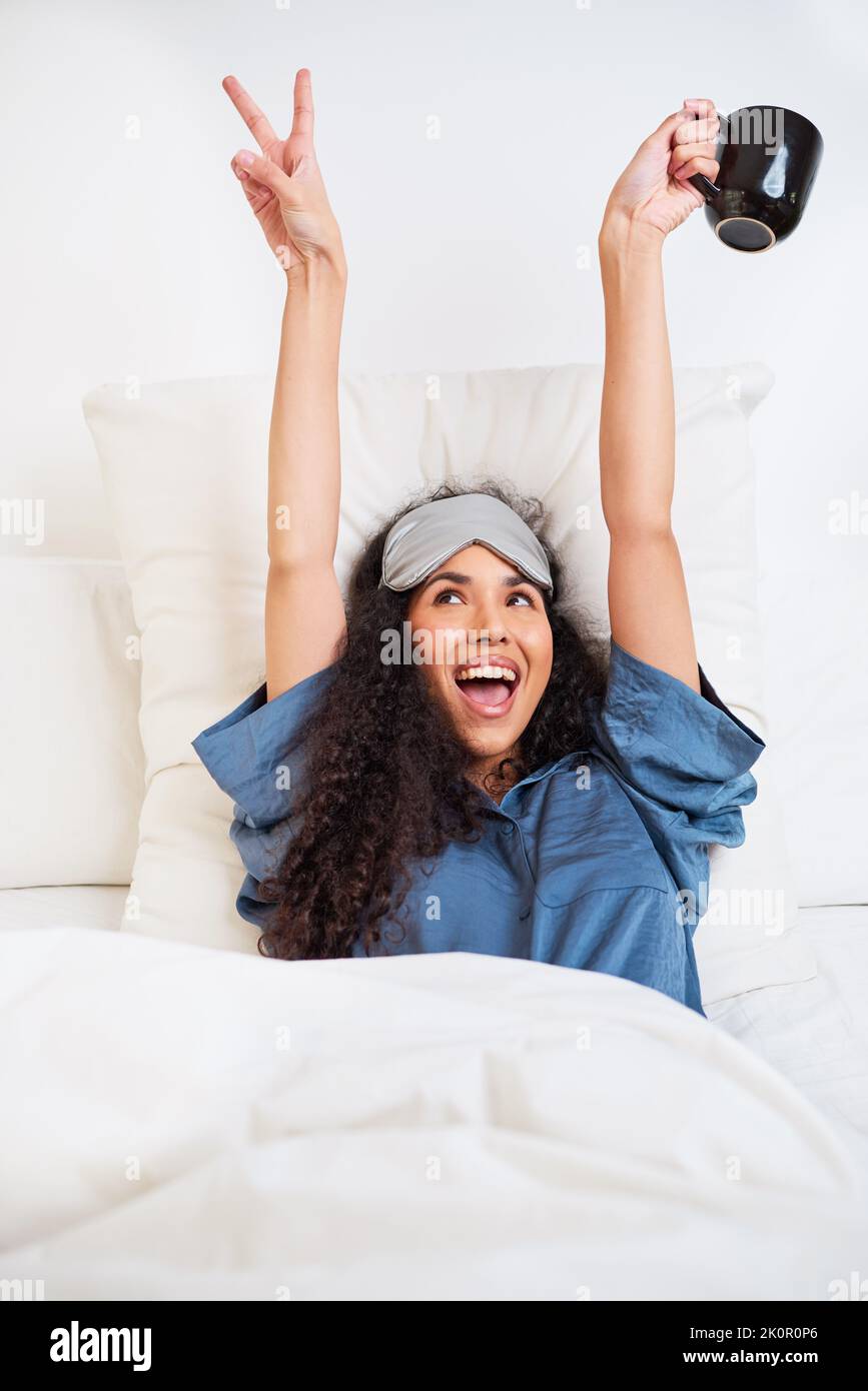 A young multi-ethnic woman shows peace sign waking up in bed with ...