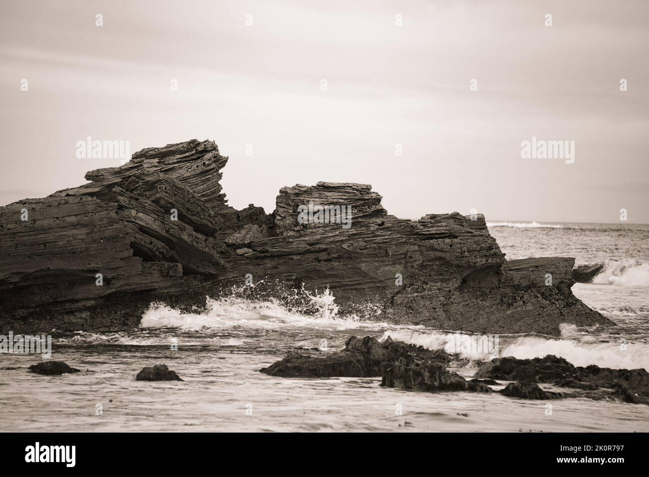A grayscale shot of sea waves crashing into the rock formations near ...