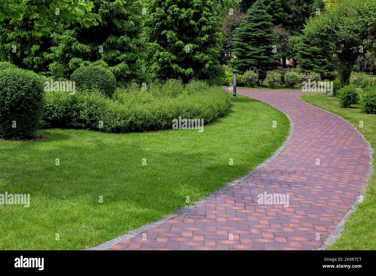 curved pathway paved brick stone tiles in park among plants, foliage ...