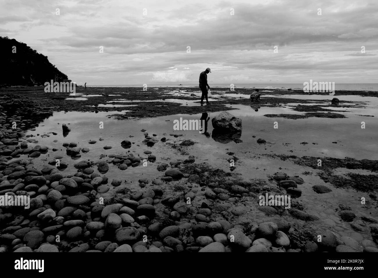A black and white shot of a person standing on a coast on a cloudy day ...