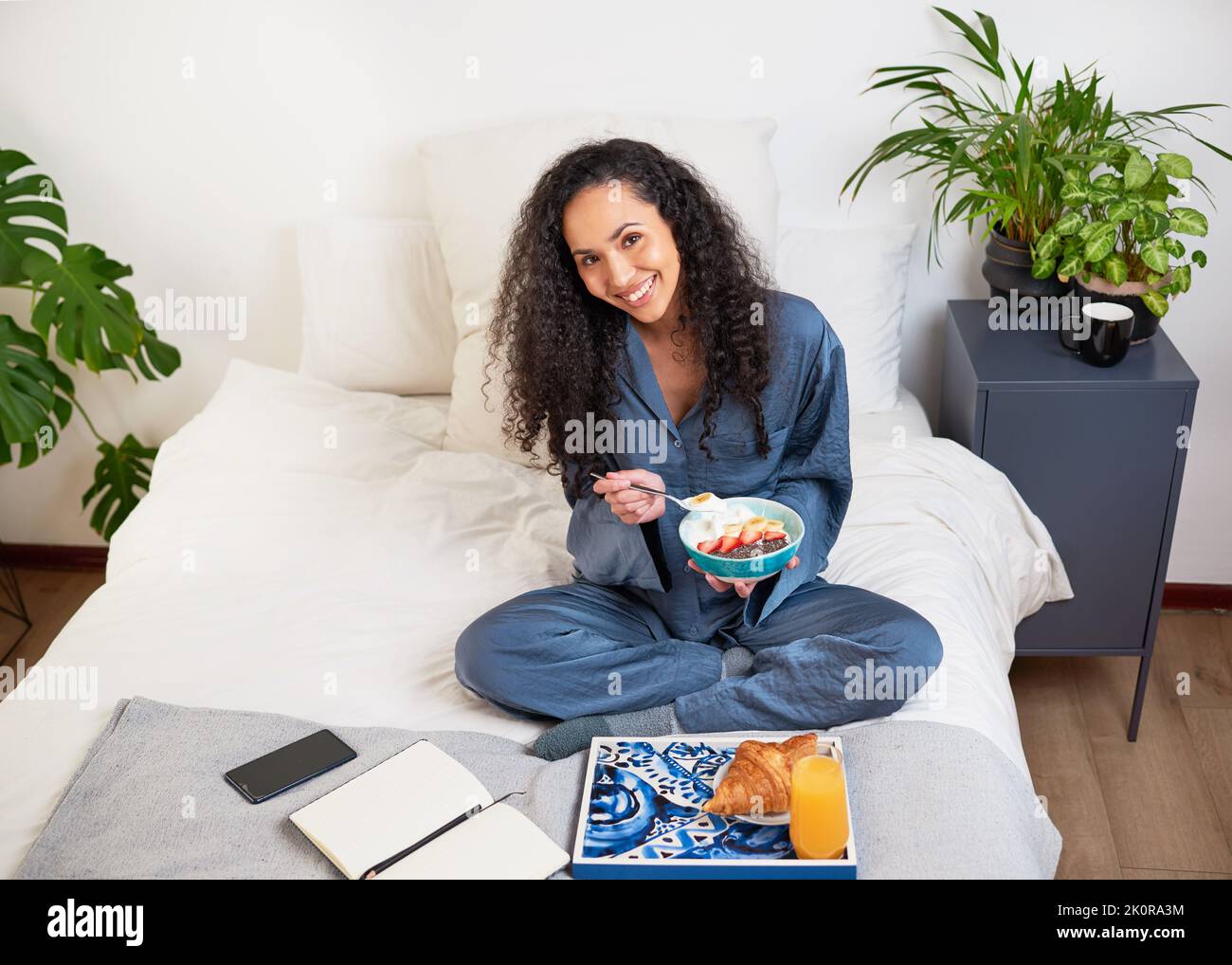 A beautiful young woman eats breakfast in bed in silk pajamas on the ...