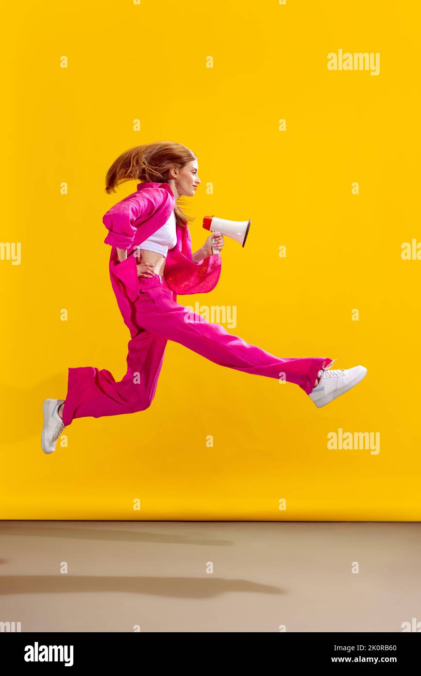 Portrait of young beautiful woman posing in a jump with megaphone ...
