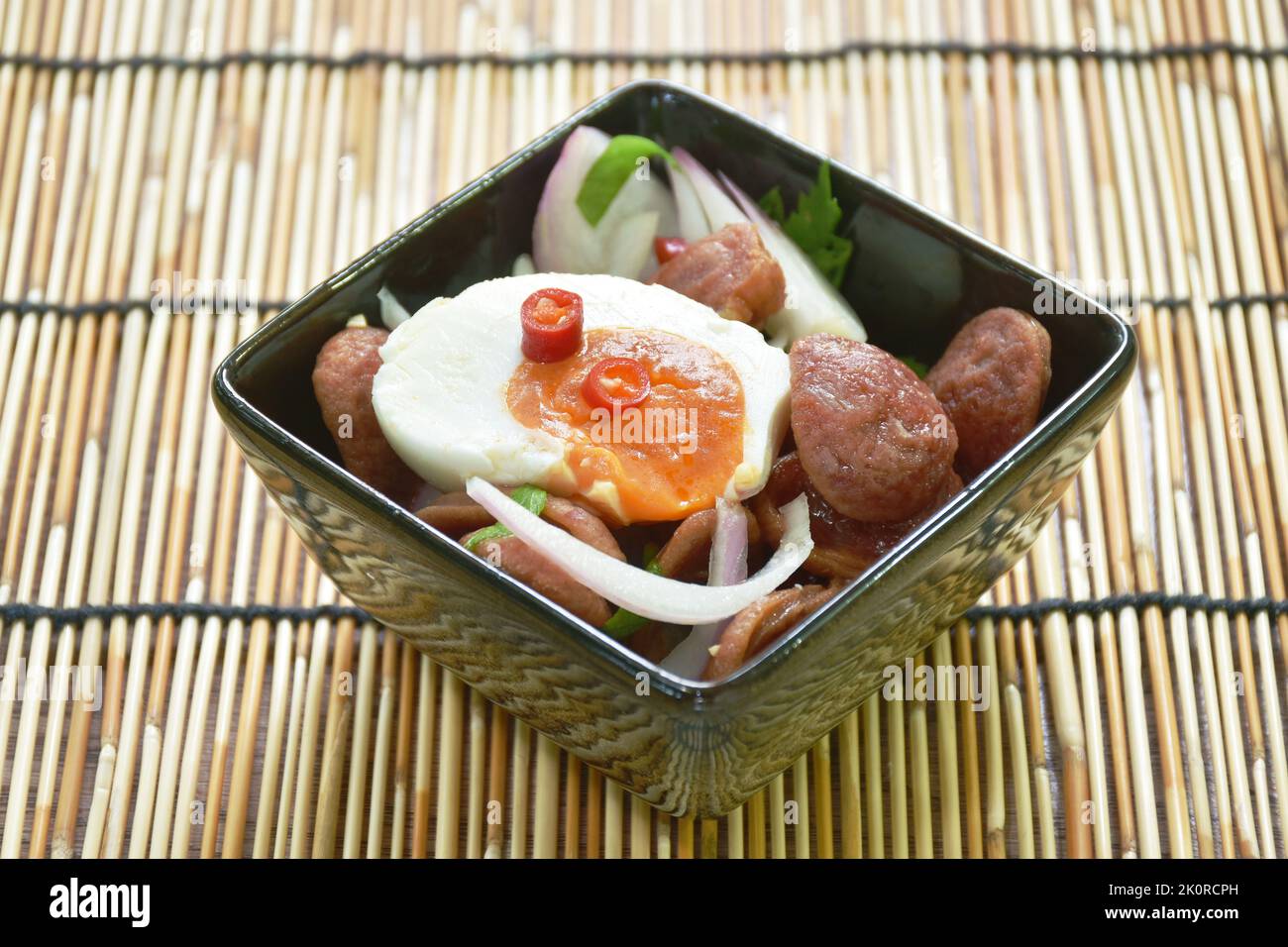 boiled spicy salty egg half cut with Chinese pork sausage topping shallot salad on bowl Stock ...