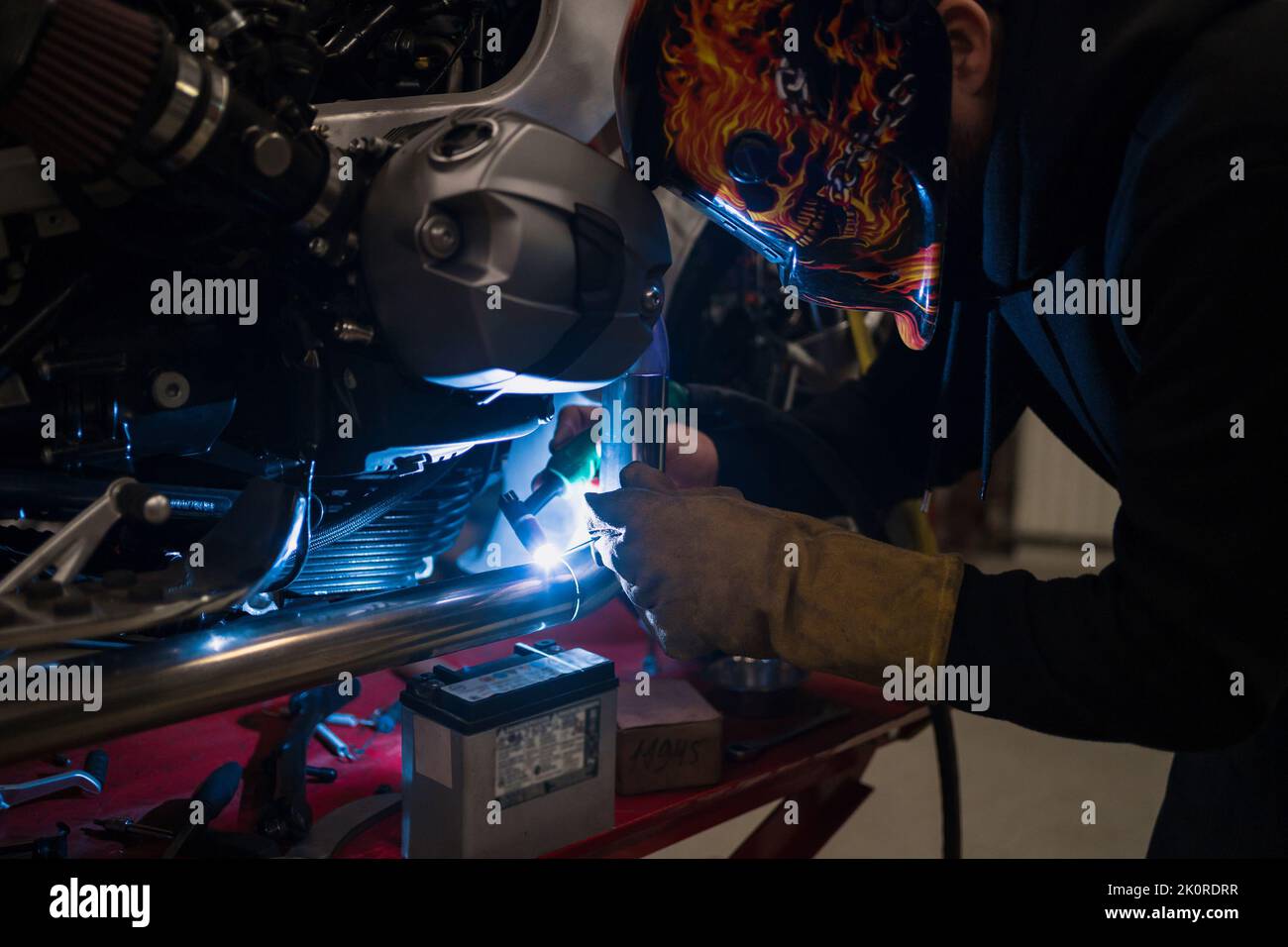 Worker in helmet with flames welding the steel part of a motorbike ...