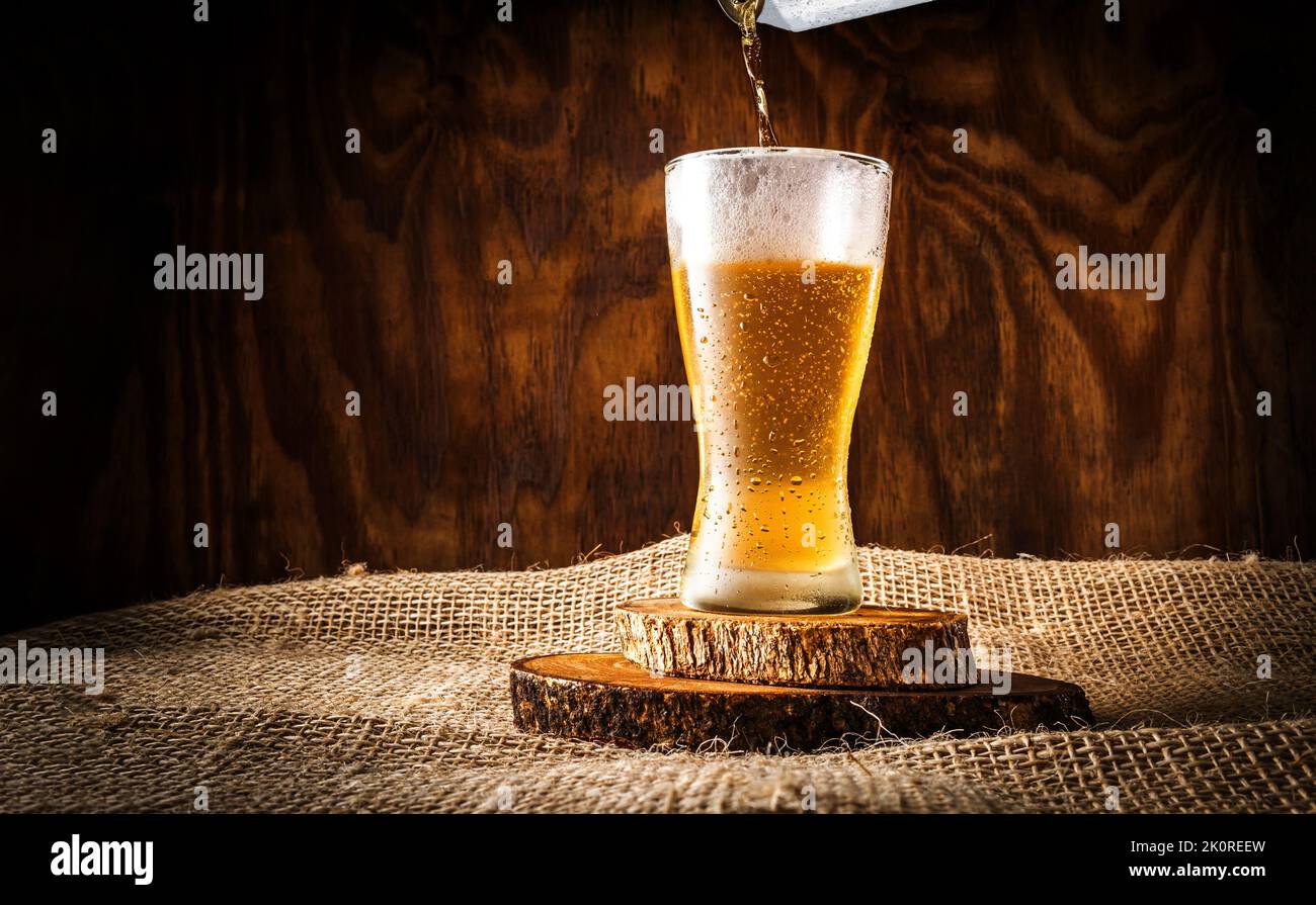 Beer pouring from a can into a glass with foam on a rustic wooden ...