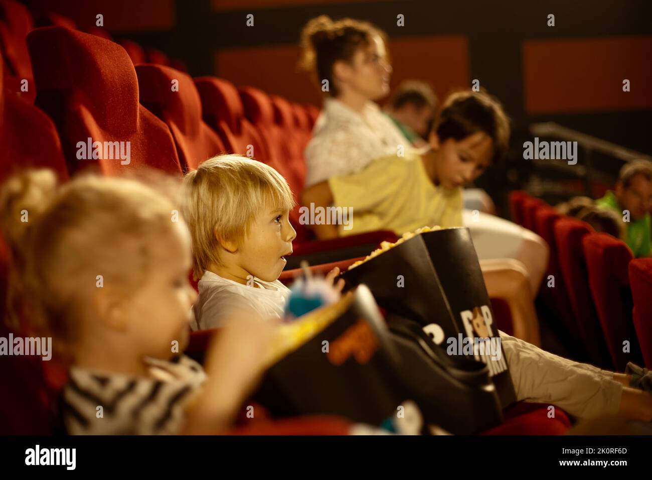 Cute child, curly girl, watching movie in a cinema, eating popcorn and ...
