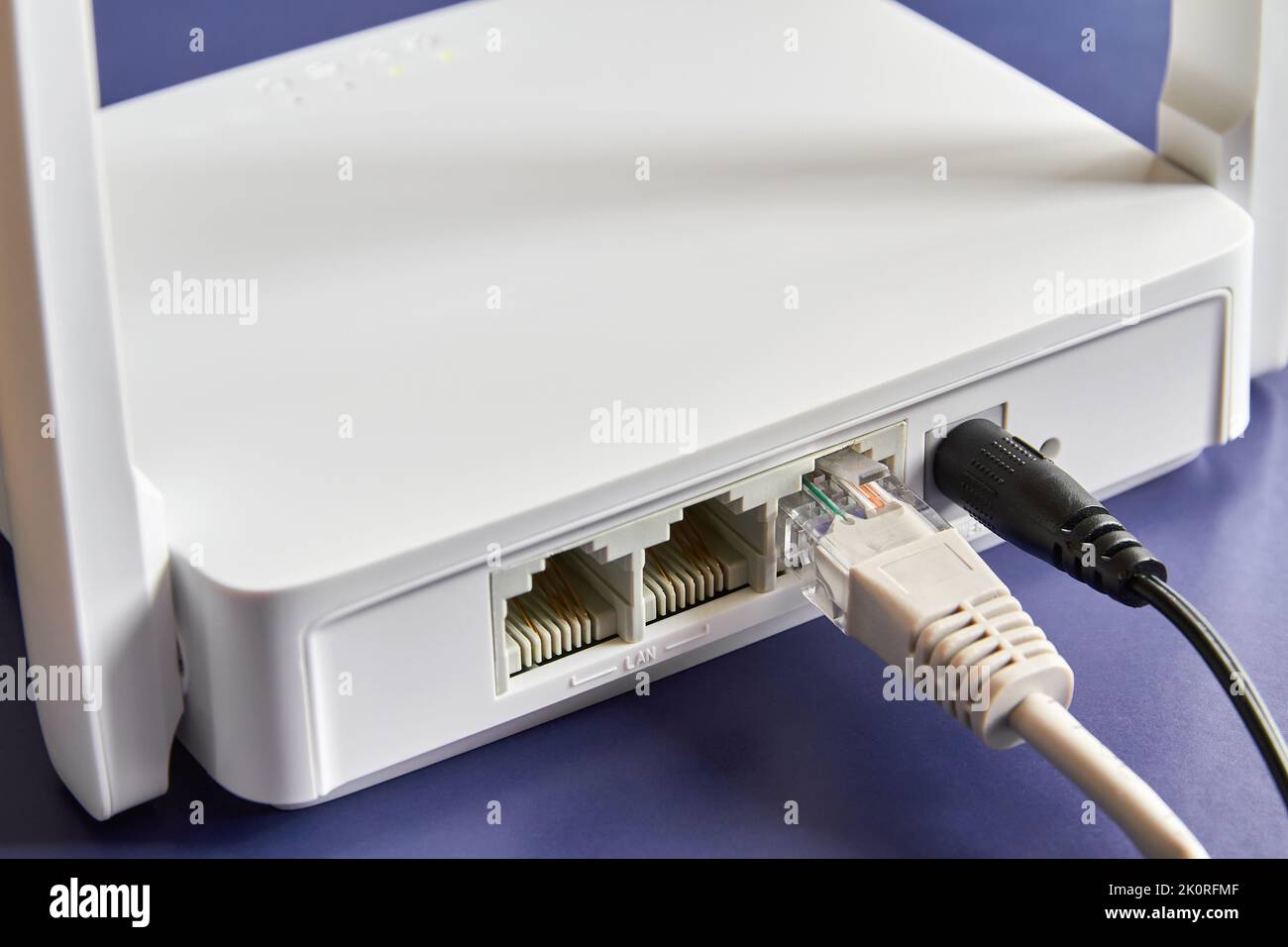 White wireless router on blue background connected by cable to the ...