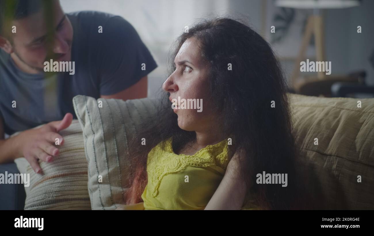 Confused woman with a disability sitting on a couch and talking with ...