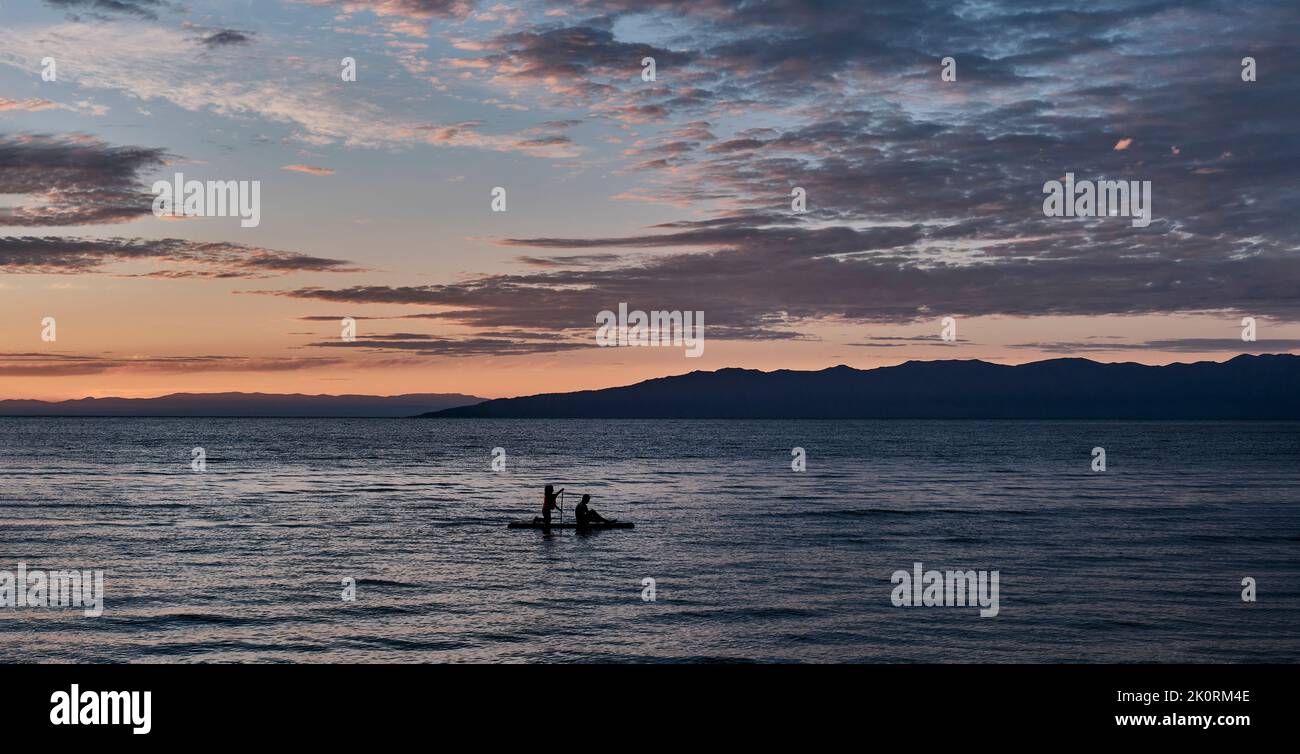 Silhouette of couple on SUP board against colorful sunset. Barguzinsky Bay of Lake Baikal ...