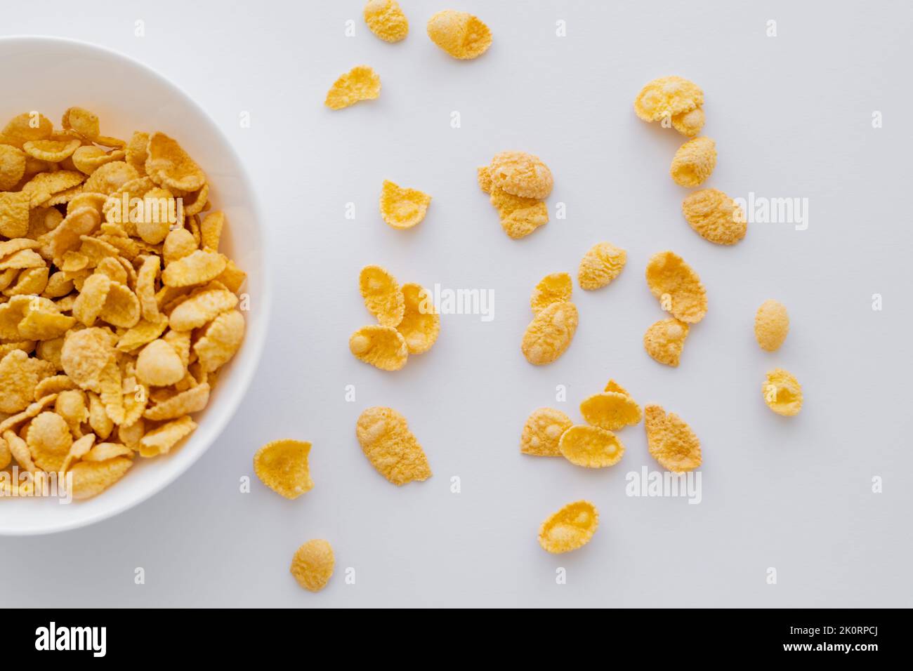 top view of crispy and yellow corn flakes near bowl isolated on white ...