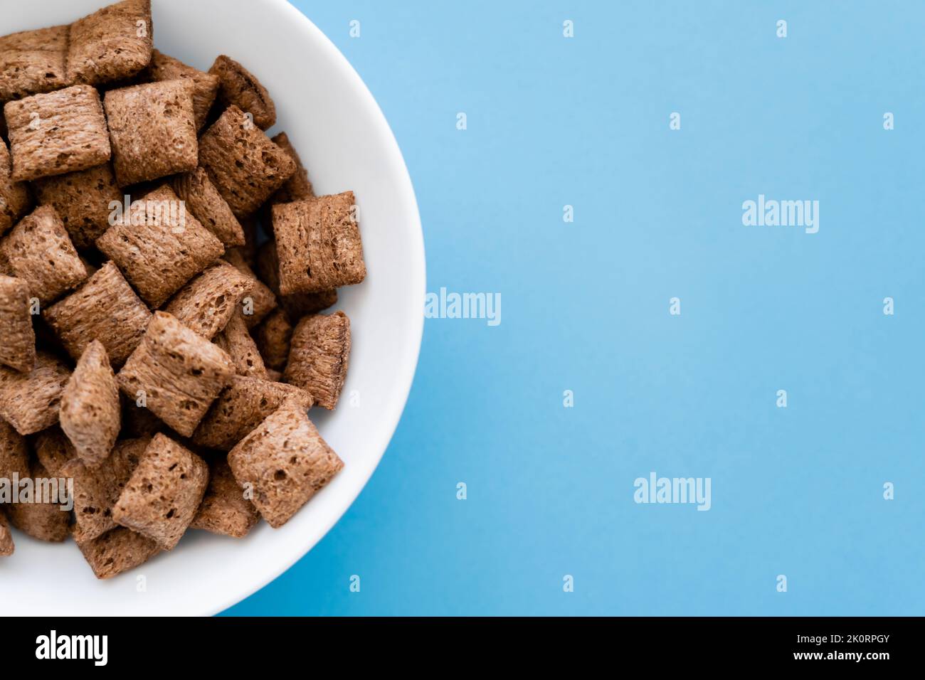 top view of chocolate cereal puffs in white bowl isolated on blue,stock ...