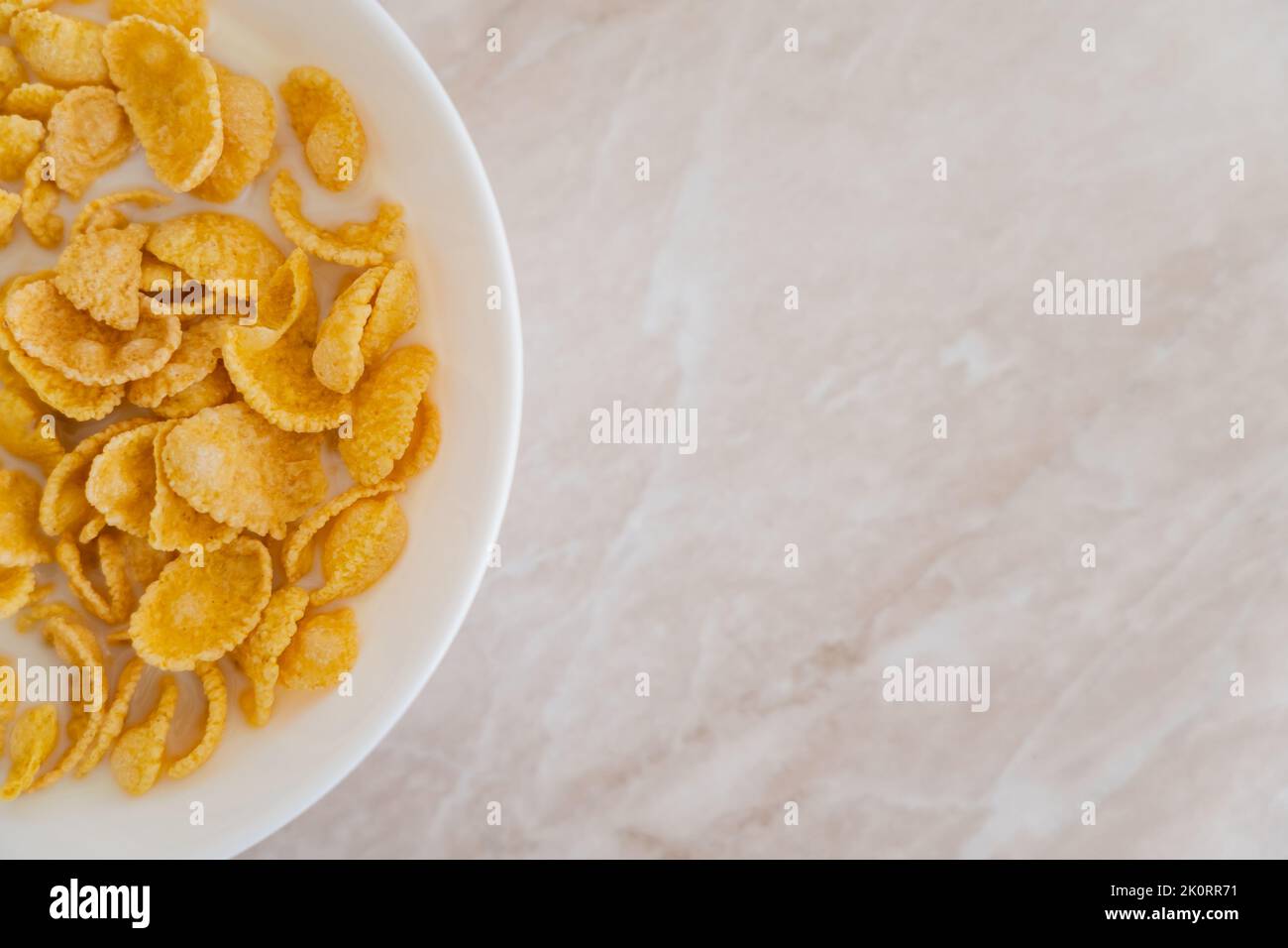 top view of crispy corn flakes in bowl with spoon and milk on marble ...