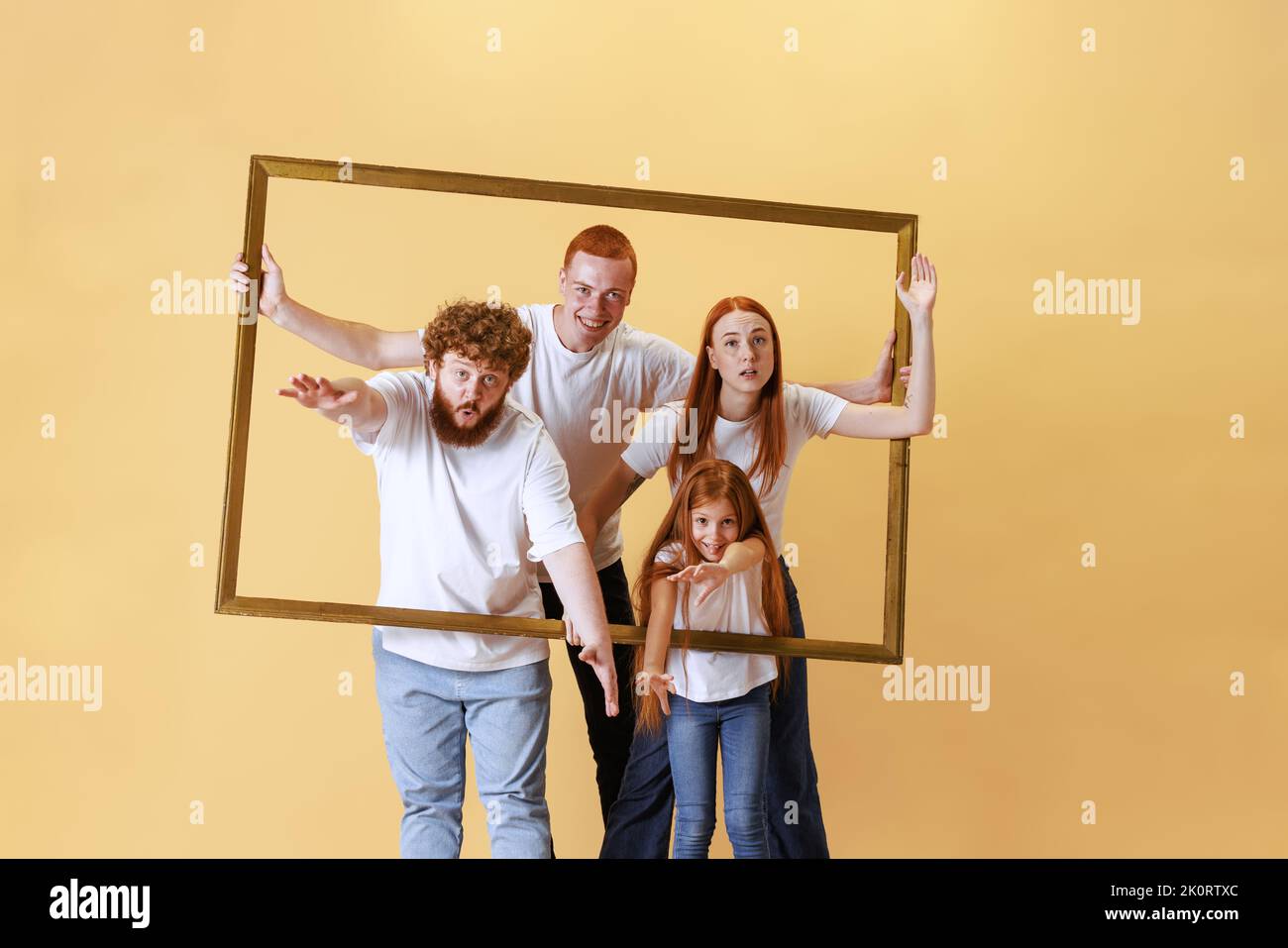 Joyful redhead family looking through picture wooden frame together ...