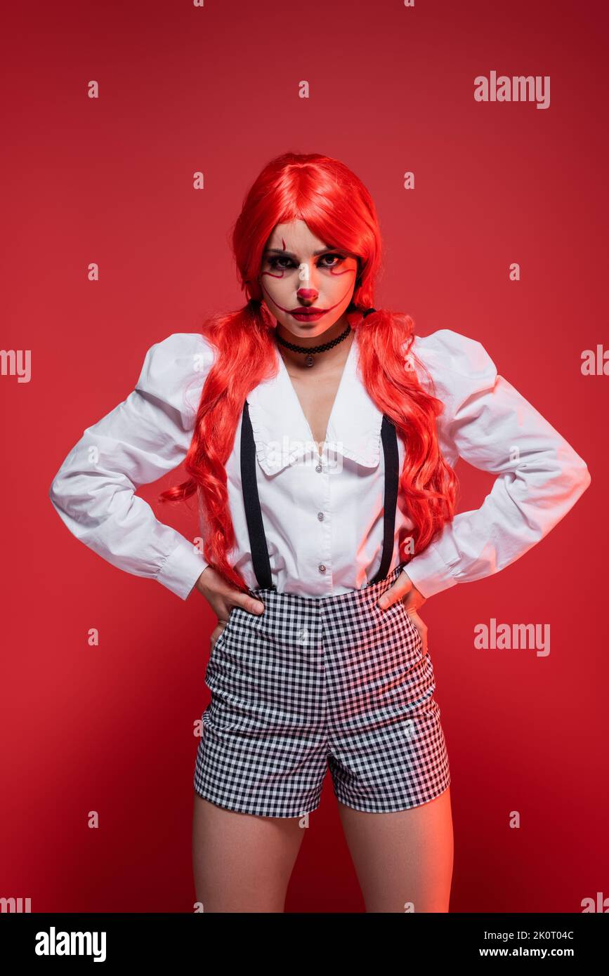angry woman with bright long hair and clown makeup standing with hands ...