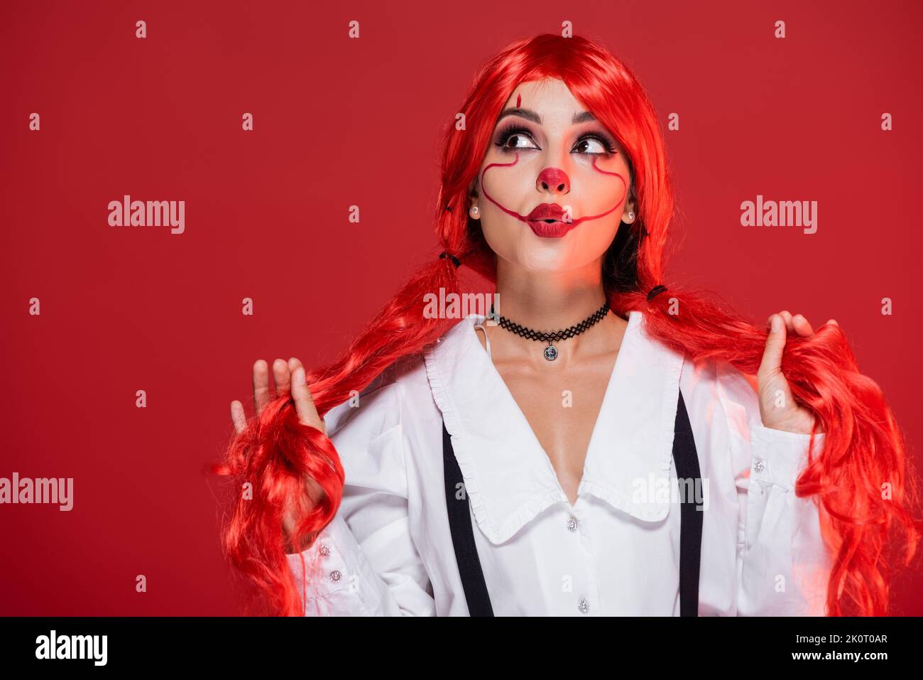 tricky woman with clown makeup holding bright ponytails and looking up ...