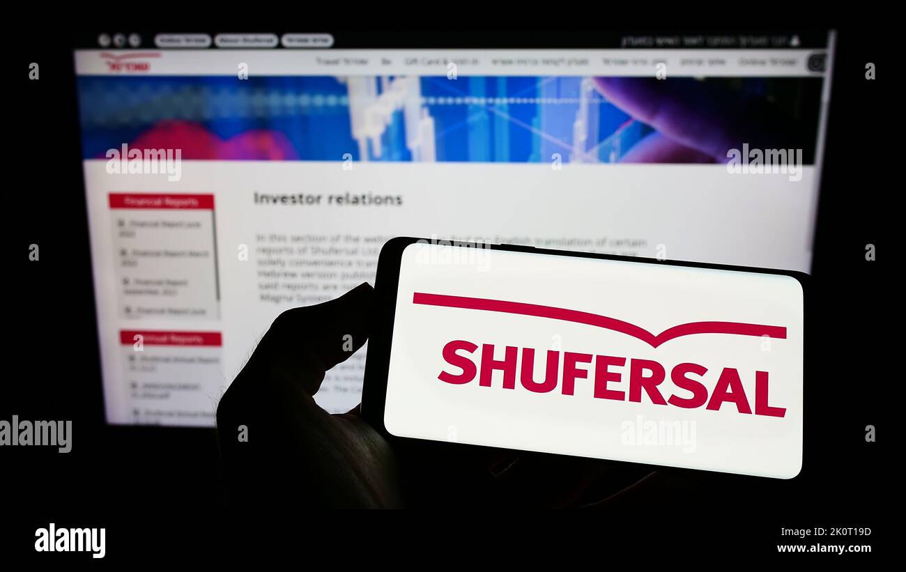 Person holding mobile phone with logo of Israeli supermarket chain Shufersal Ltd. on screen in ...