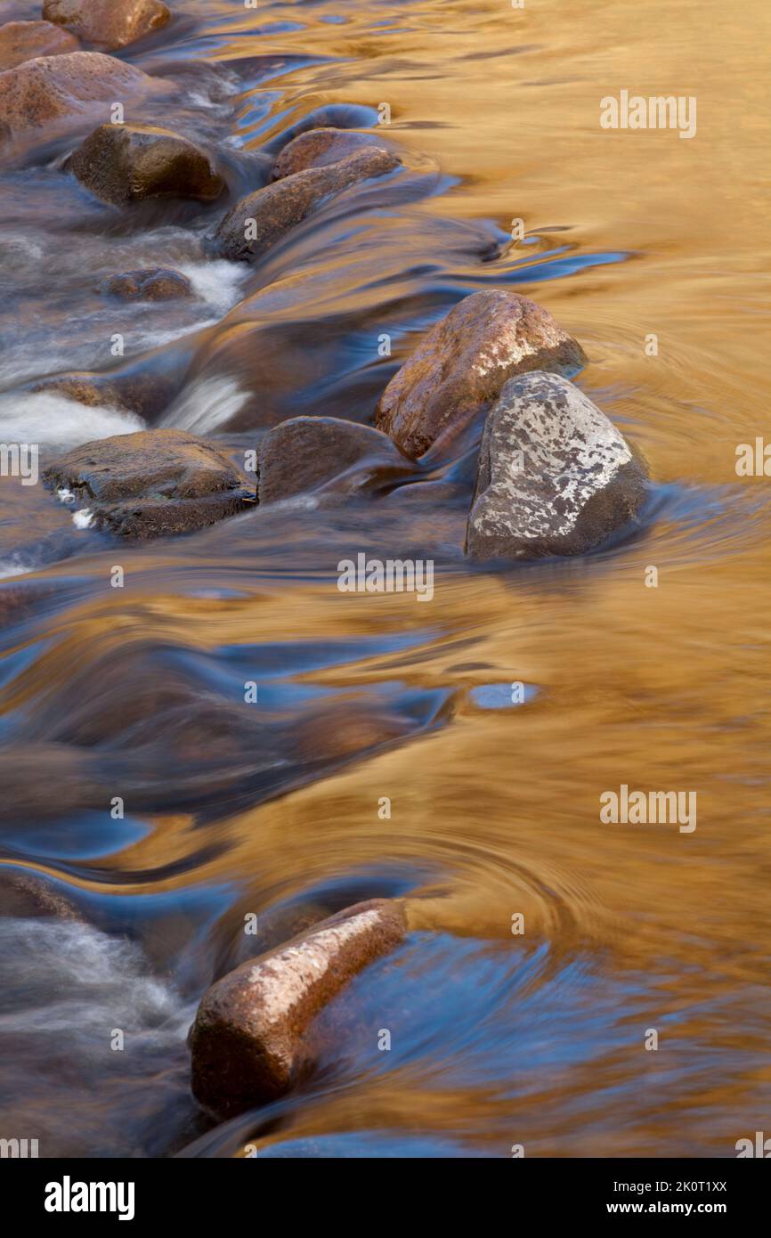 Thw waters of a small river flow gently over rocks with the reflection ...