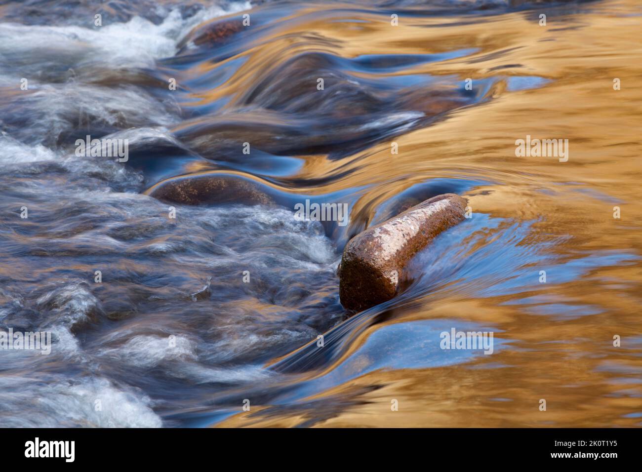 Thw waters of a small river flow gently over rocks with the reflection ...