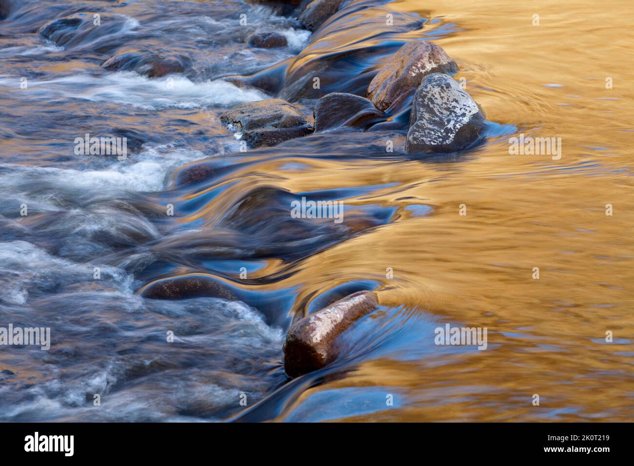 Thw waters of a small river flow gently over rocks with the reflection ...