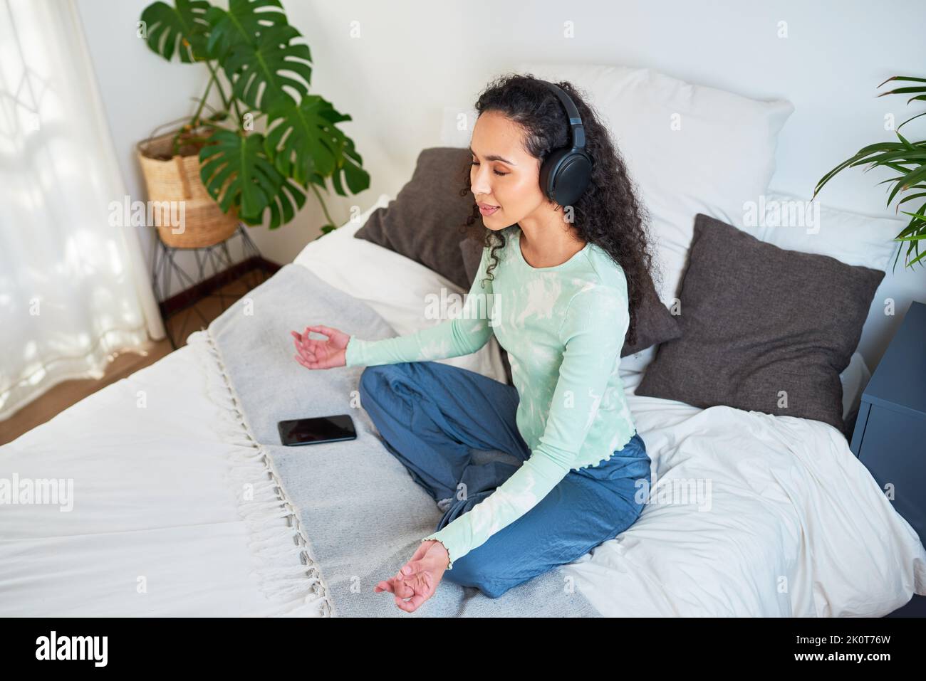 A young multi-ethnic woman sits on her bed meditating with mindfulness ...