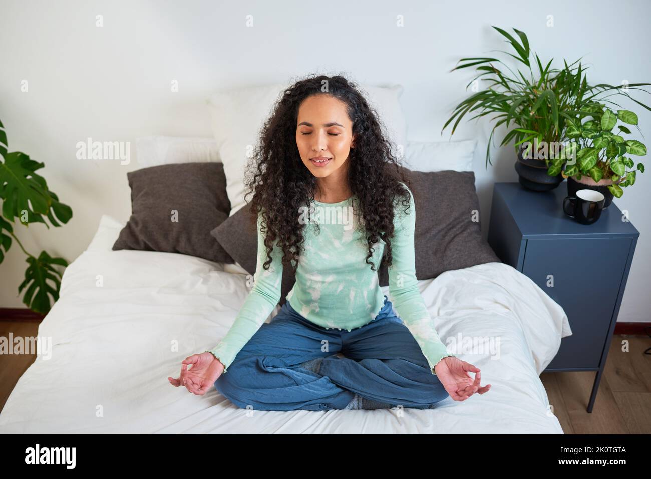 A young multi-ethnic woman sits cross-legged meditating in bed Stock ...