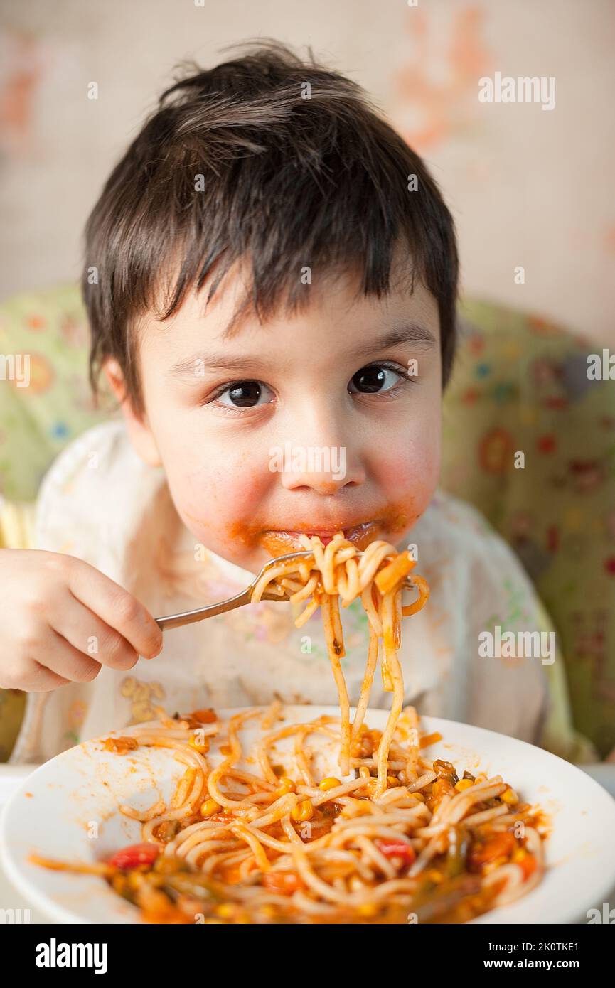 Child eating spaghetti with vegetables. Kid having fun eating. Brown ...