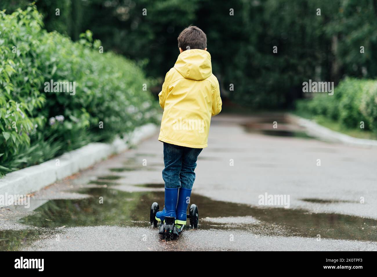 Little boy in raincoat and rubber boots playing in puddle. Fun on ...