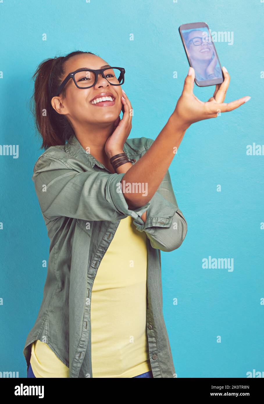 Be your selfie. a young woman taking a selfie against a blue background ...