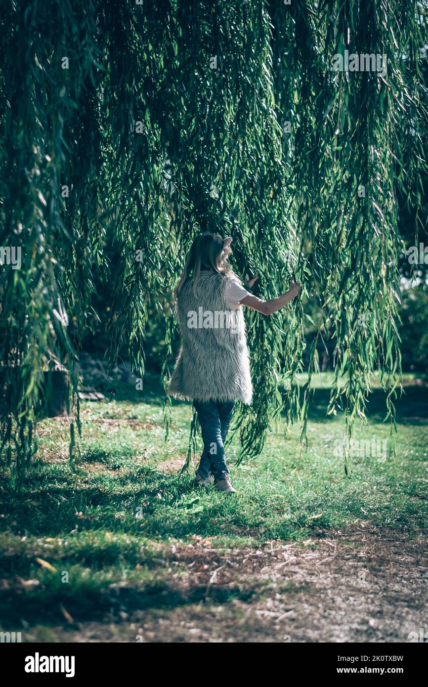 cute teenage girl with long blond hair having fun with willow tree in ...